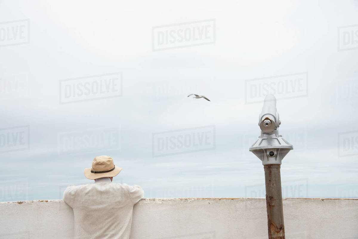 Man peering over a wall beside a telescope along the Algarve coast of ...