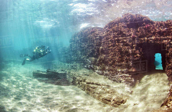 Scuba diver swimming through submerged ancient Roman building ruins ...