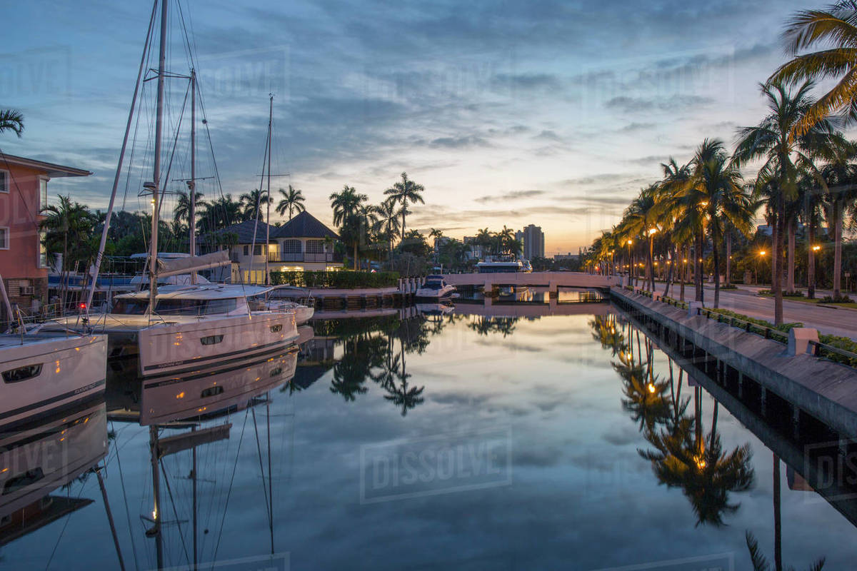 View along tranquil canal at dawn, yachts reflected in still water ...