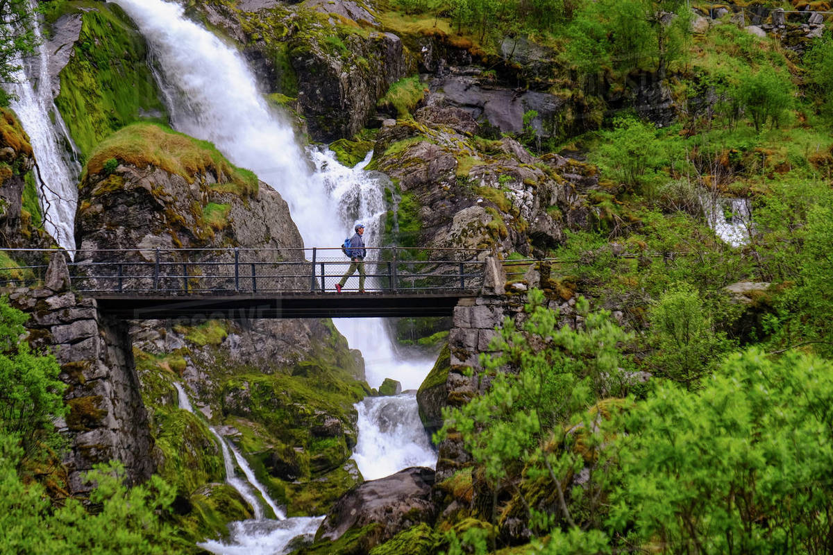 A man on a pedestrian bridge crosses one of many waterfalls originating ...