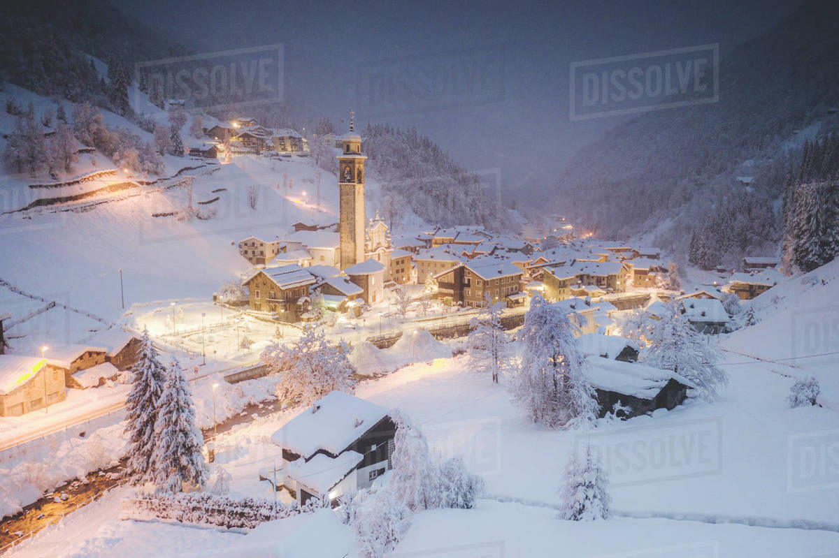 Illuminated village of Gerola Alta and frozen river covered with snow ...