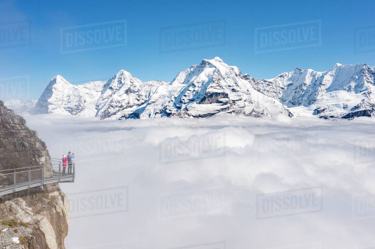 Two people photographing snowcapped Eiger and Monch peaks in fog from ...