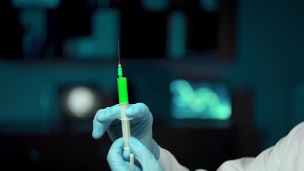 Hand tapping syringe, preparing needle for injection. Dark background ...