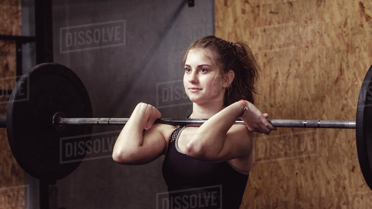 Strong muscular young woman working out with a barbell weight lifting ...