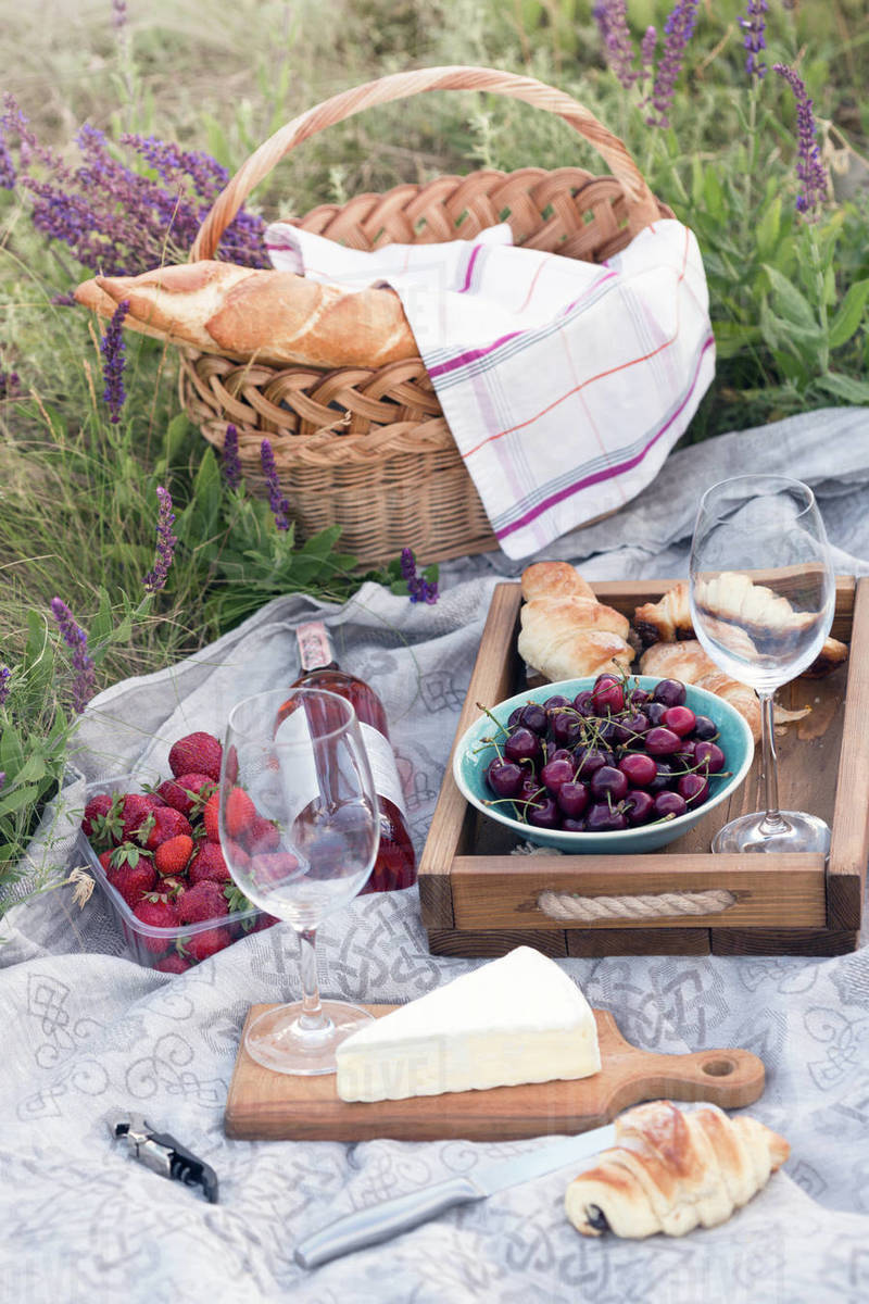 Summer - picnic in the meadow. Cheese brie, baguette, strawberry, cherry, wine, croissants and ...