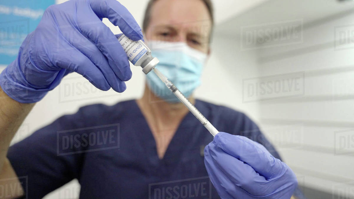 wide shot of a male healthcare worker filling a syringe with a covid-19 ...