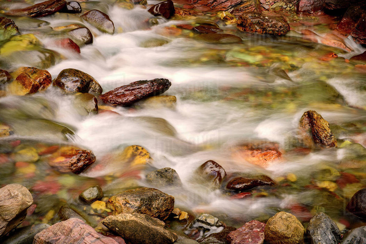 Colorful rocks in a rushing mountain stream. Glacier National Park ...