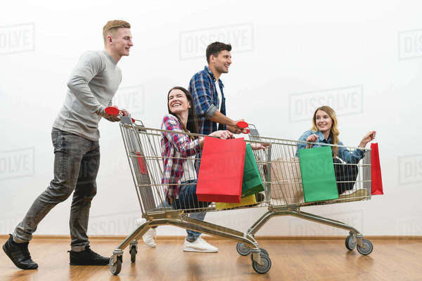 The four happy people ride on the cart on a white wall background ...