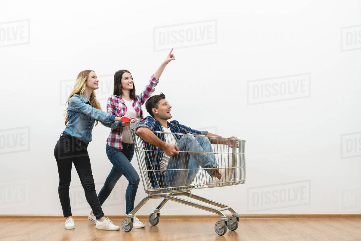 The three happy people with a shopping cart gesture on a white wall ...