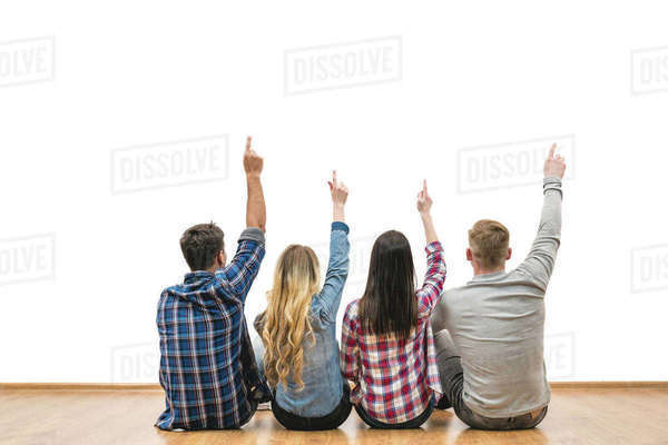 The four people sit on the floor and gesture on a white wall background ...