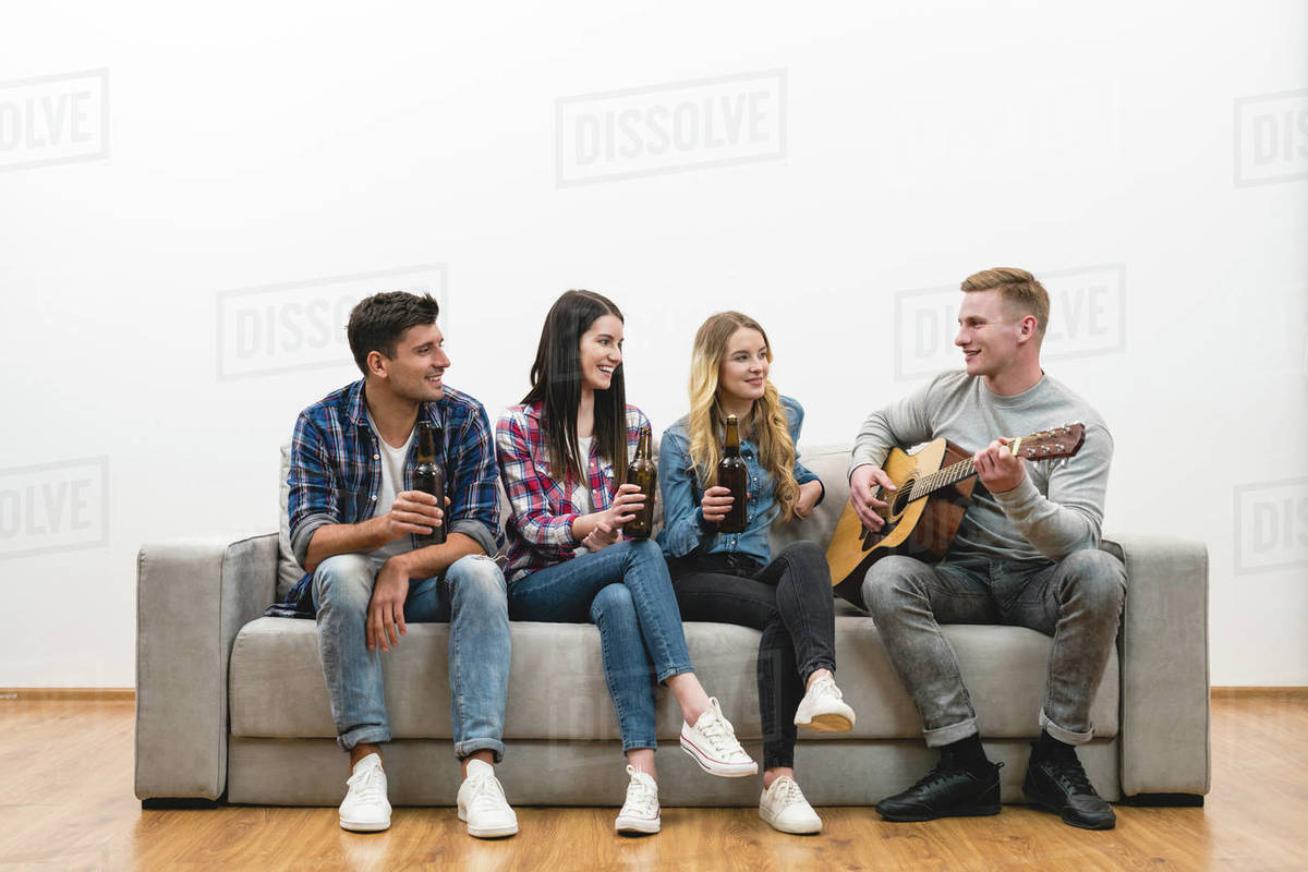 The four friends drink a beer and play the guitar on the white wall ...