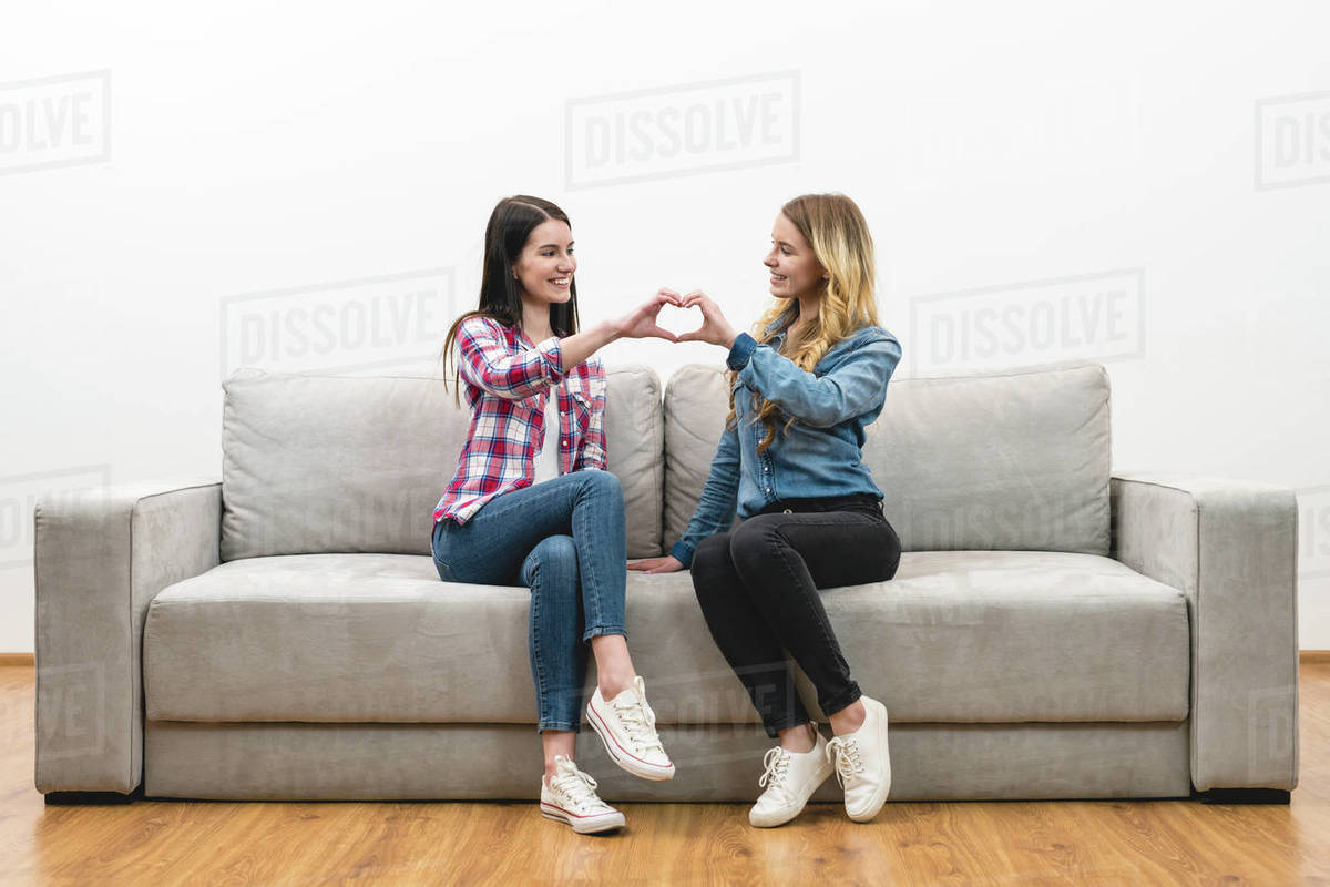 The two women show the heart symbol on the white wall background ...