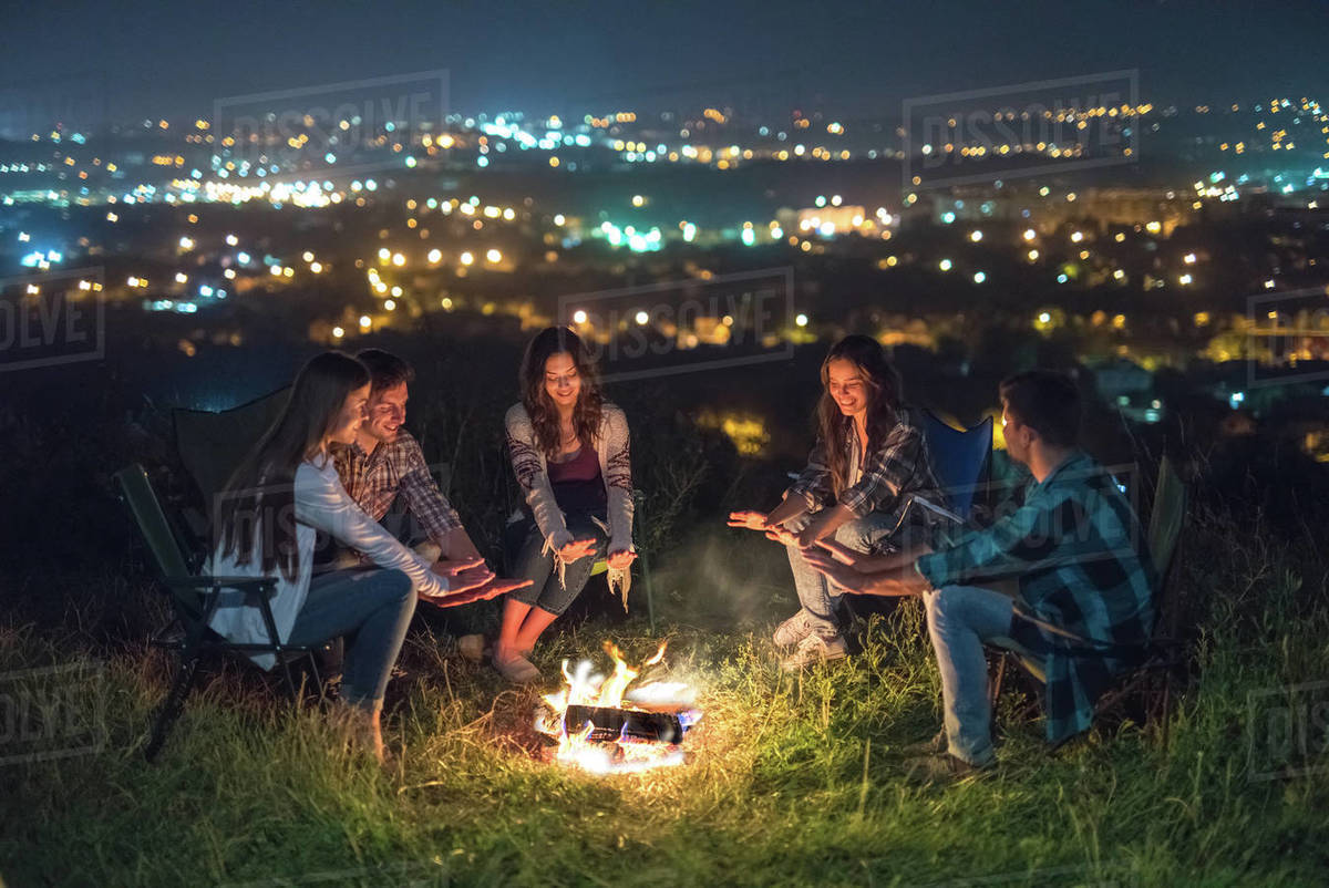 The young people warming near a bonfire on a city lights background ...
