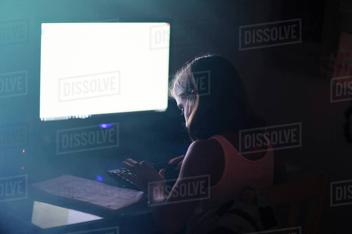 Girl using computer in dimly-lit room - Stock Photo - Dissolve
