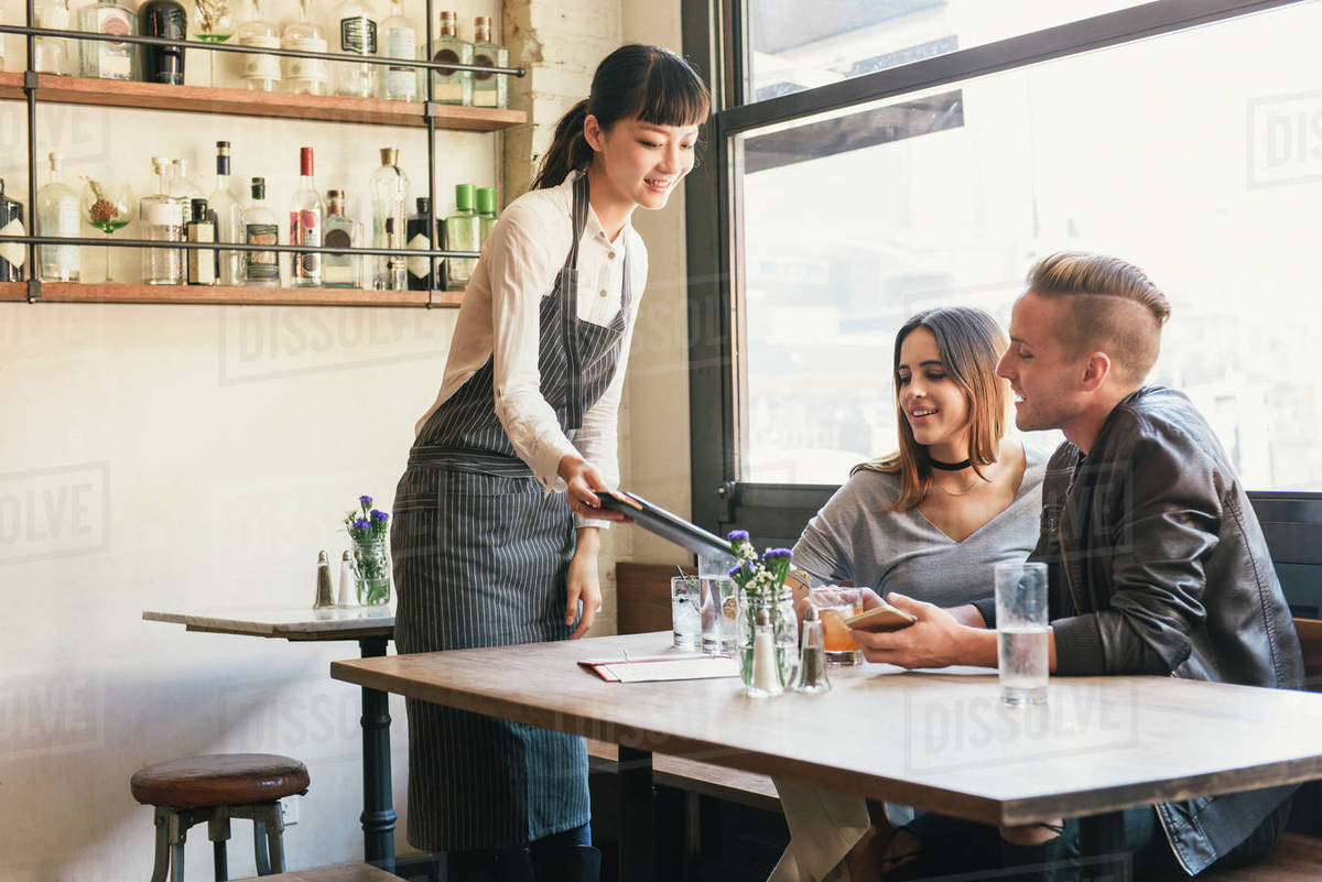 Female bartender handing bill to young couple at cocktail bar table ...
