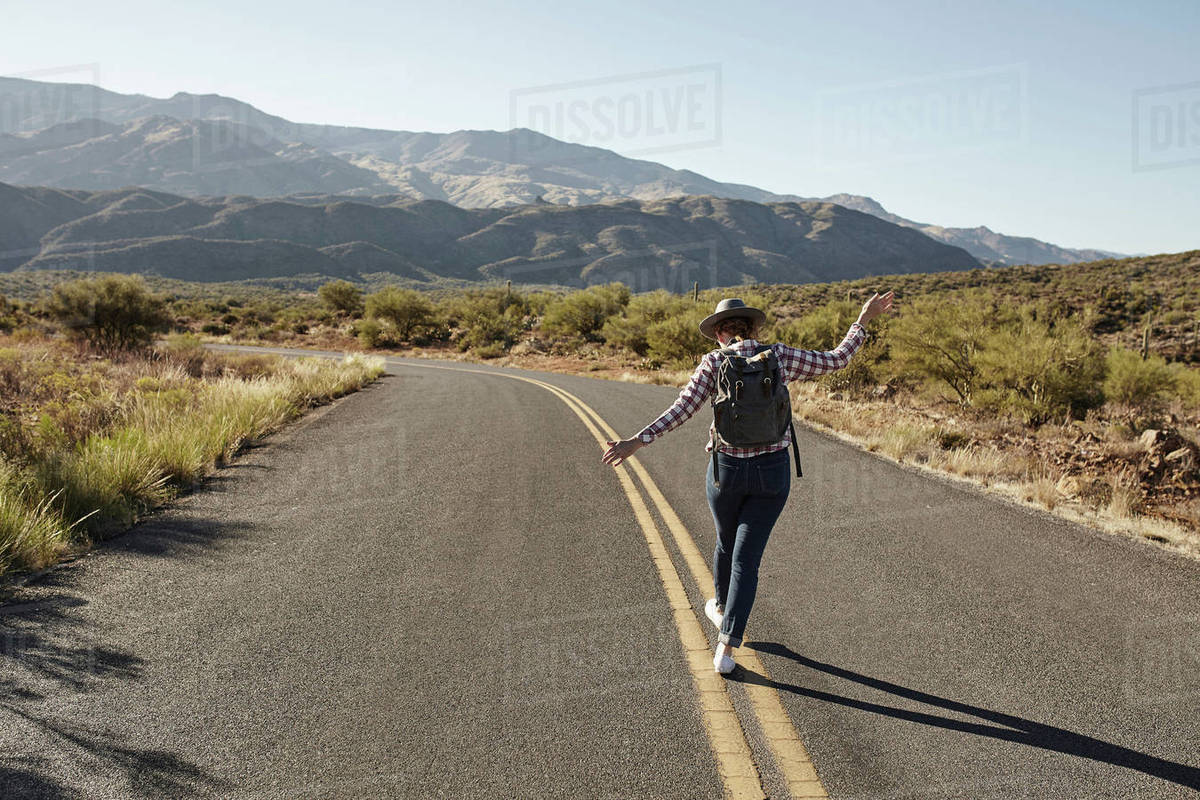 Woman walking along road markings of desert road, rear view, Sedona ...