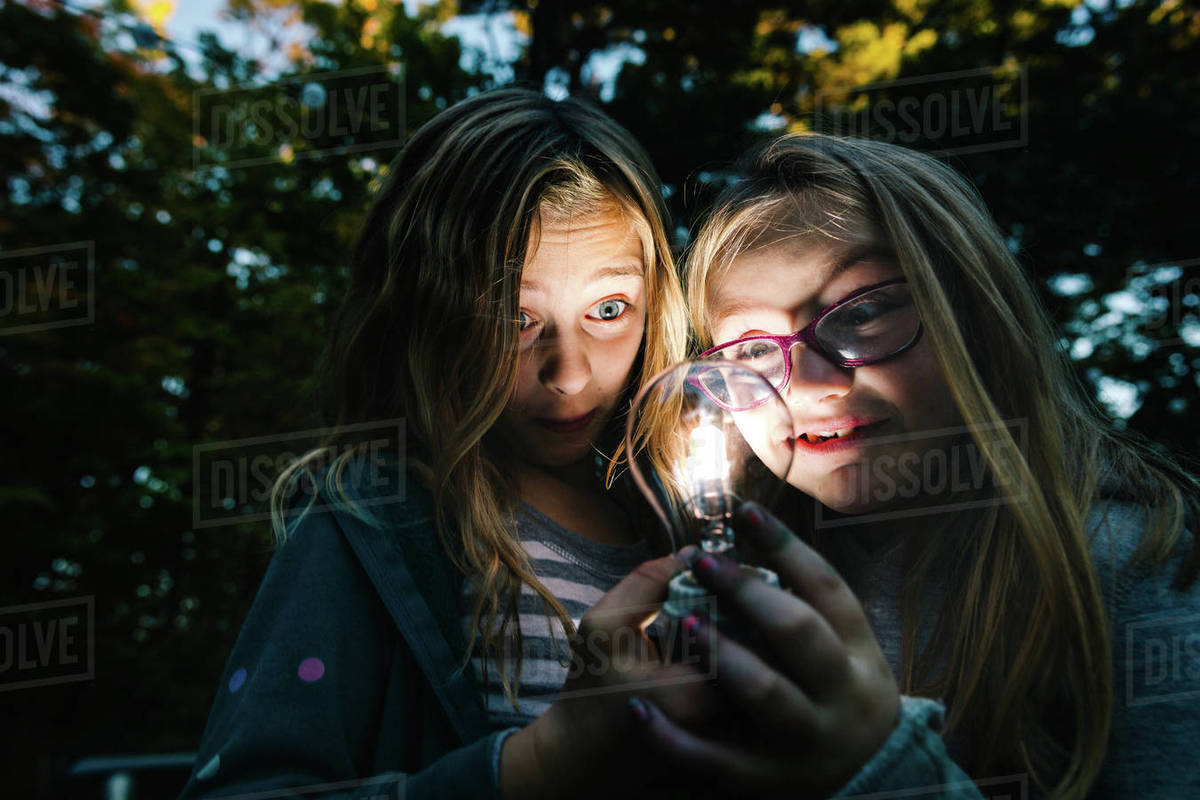 Two girls holding and staring at illuminated lightbulb in garden at ...