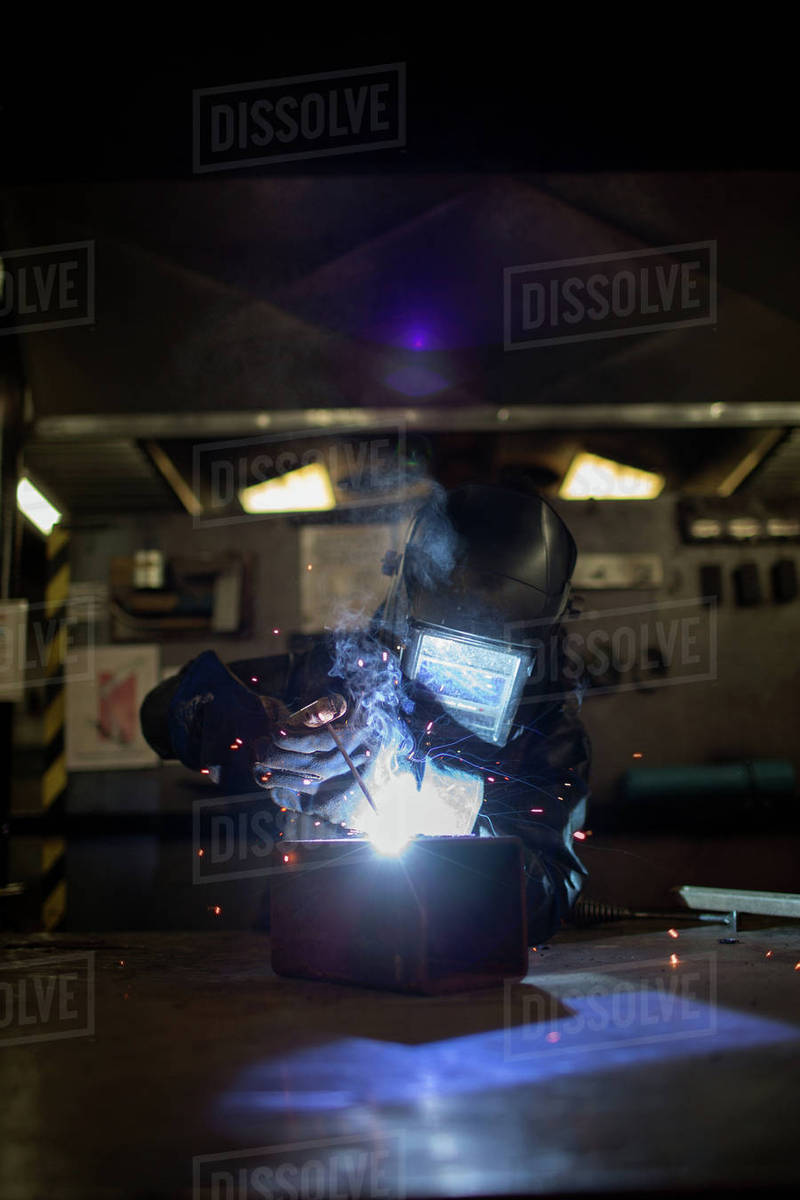 Female metalsmith welding metal box on workbench - Stock Photo - Dissolve