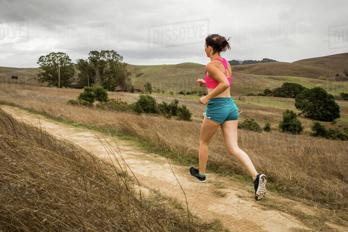 Female runner running on dirt track in landscape - Stock Photo - Dissolve