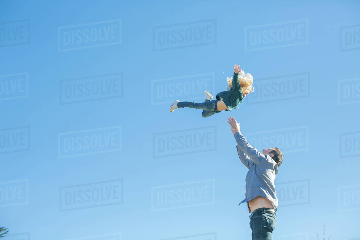 Girl being thrown mid air by father against blue sky - Royalty-free ...