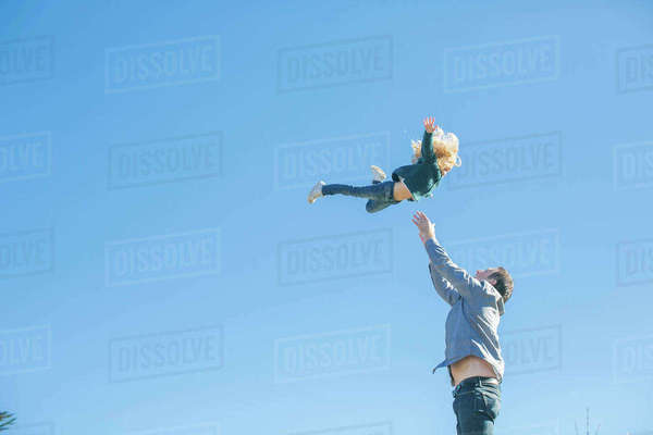 Girl being thrown mid air by father against blue sky - Royalty-free ...