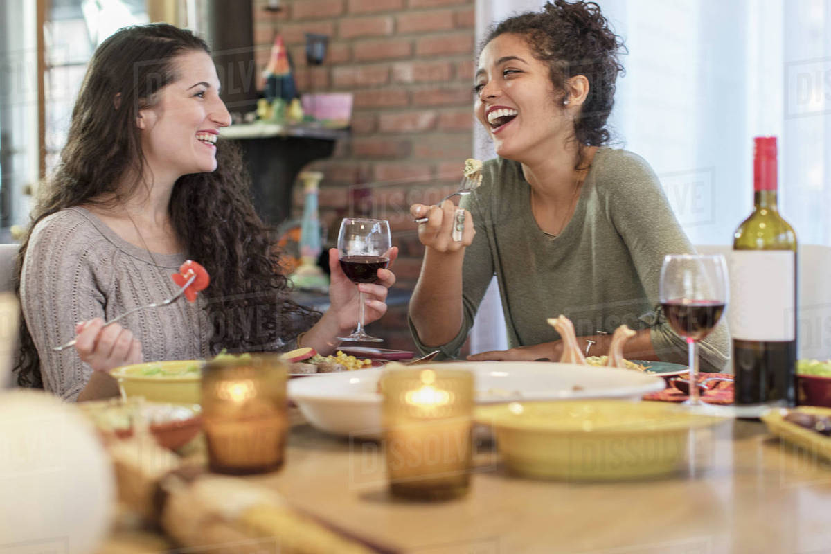 Two young women friends eating meal at kitchen table - Royalty-free ...