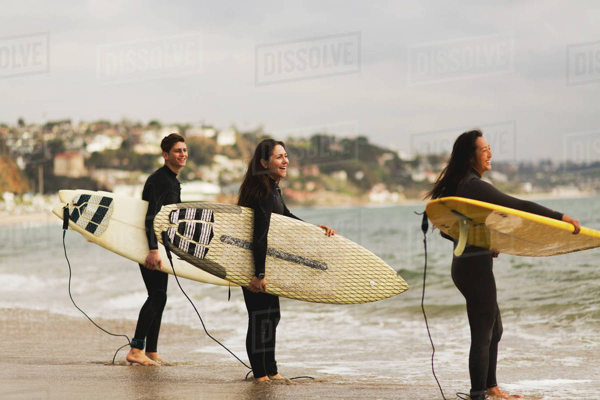 Three friends standing in sea, holding surfboards, preparing to surf ...