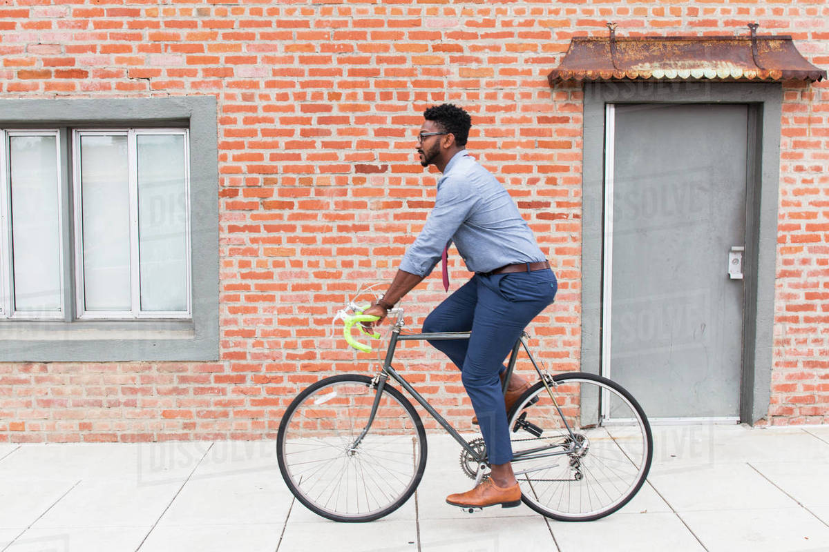 Side view of young man cycling along sidewalk - Royalty-free Stock ...