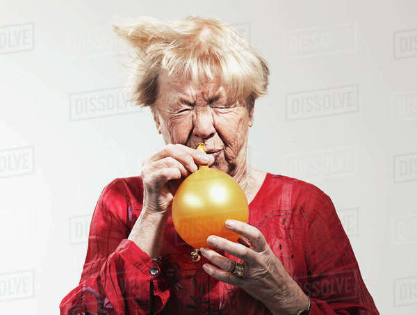 Senior woman deflating a balloon against white background - Royalty ...