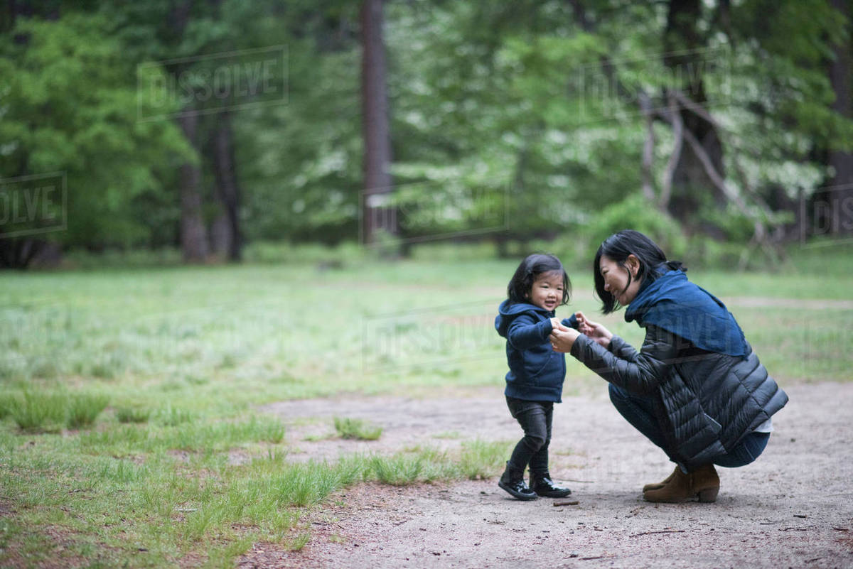 Mid adult woman crouching with toddler daughter on forest path ...