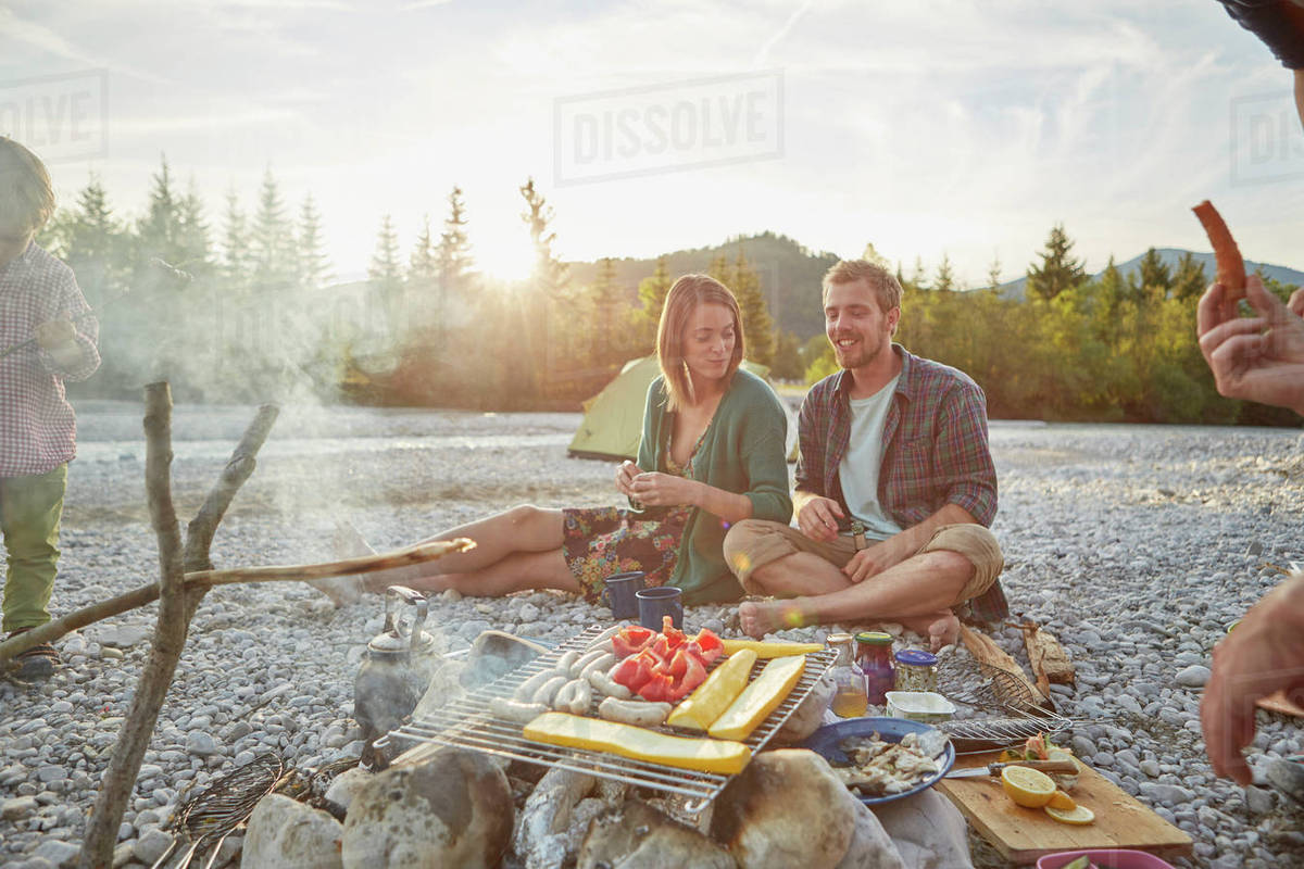 Family sitting around campfire cooking food on barbecue - Royalty-free ...