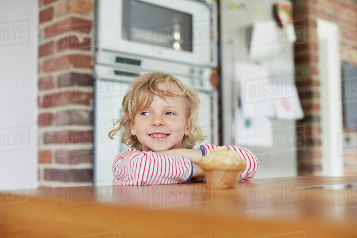 Young boy standing by kitchen counter, with muffin on counter in front ...