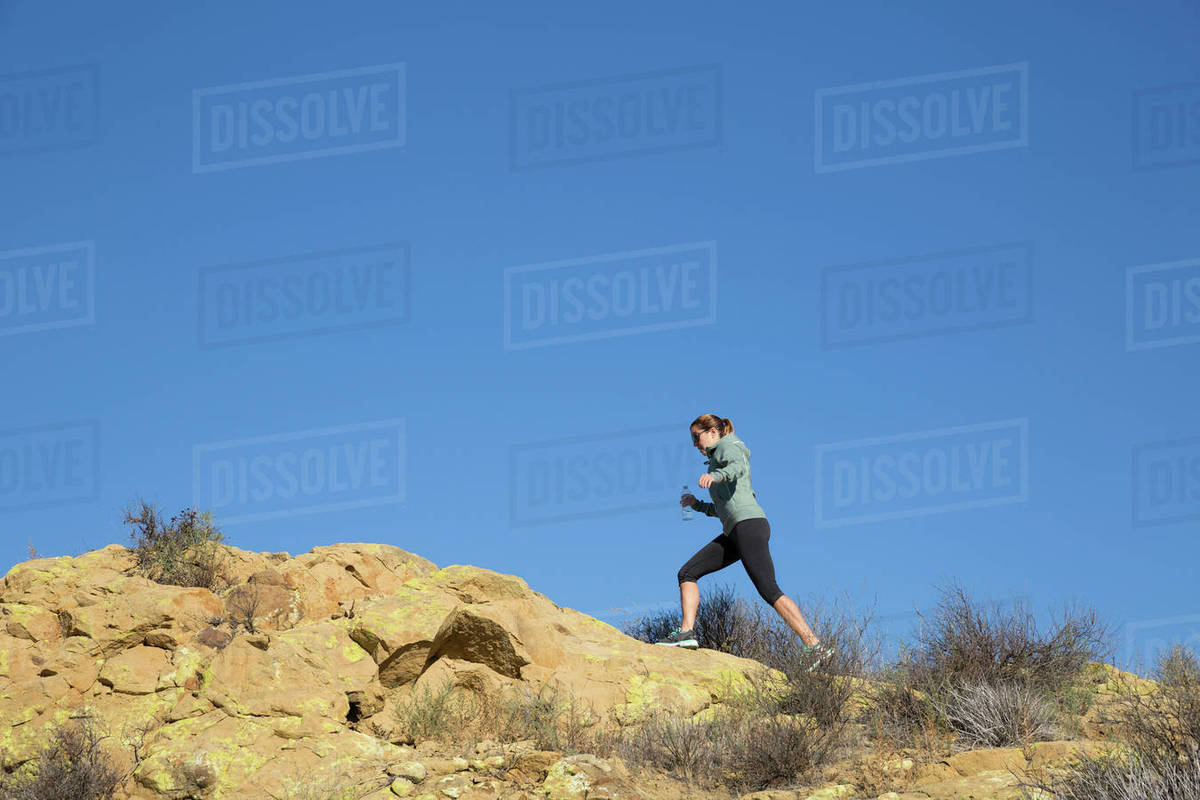 Female runner running up rugged hill - Stock Photo - Dissolve