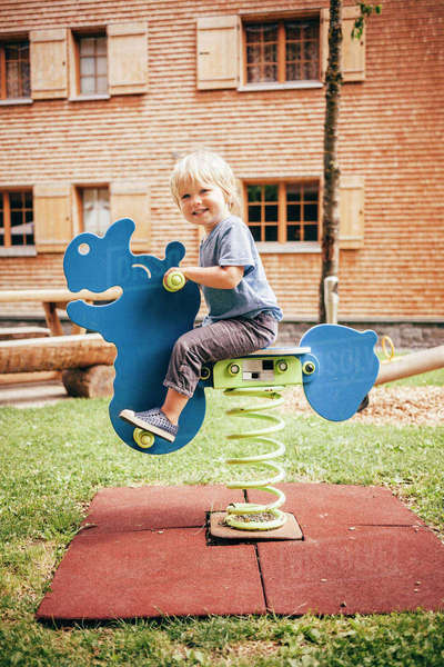 Side view of boy in playground sitting on spring rider looking at ...