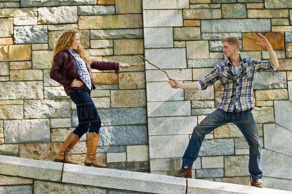 Couple play fighting with sticks against stone wall - Stock Photo ...