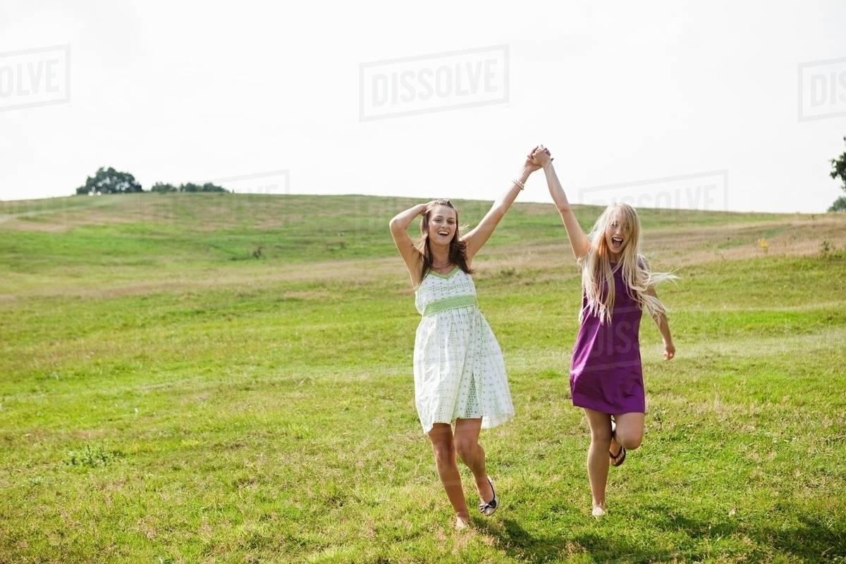Young women skipping through field with arms raised and hands held ...