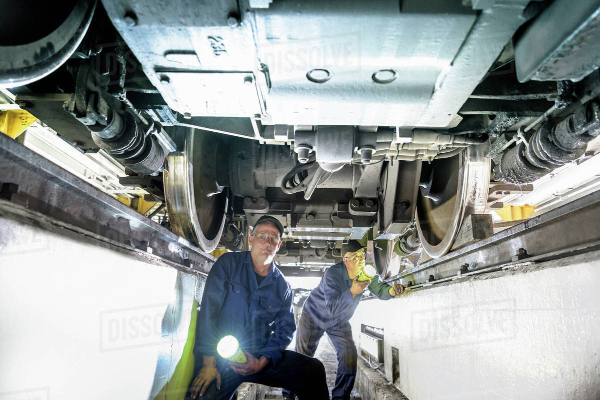 Locomotive engineers inspecting underside of locomotive in train works ...