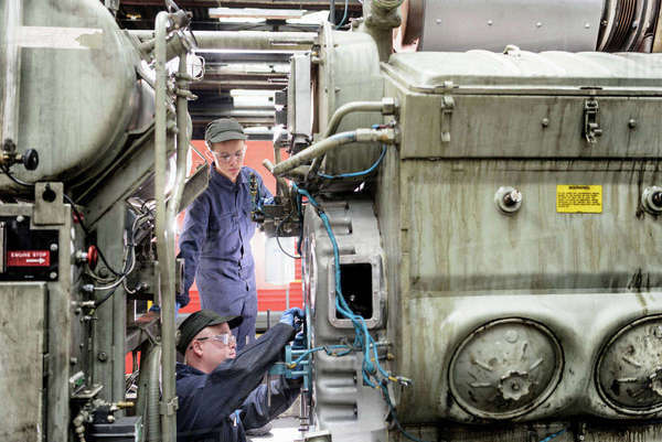 Apprentice watching engineer working on locomotive engine in train ...