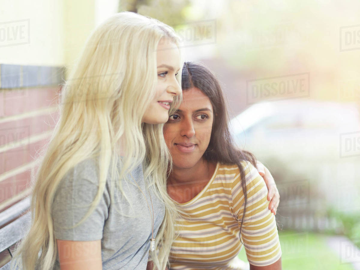 Young woman sitting on bench, hugging friend sitting beside her ...