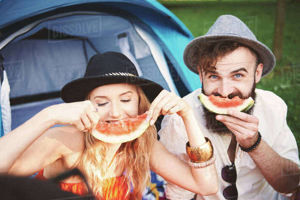 Young couple in trilbies making smiley face with melon slice at ...