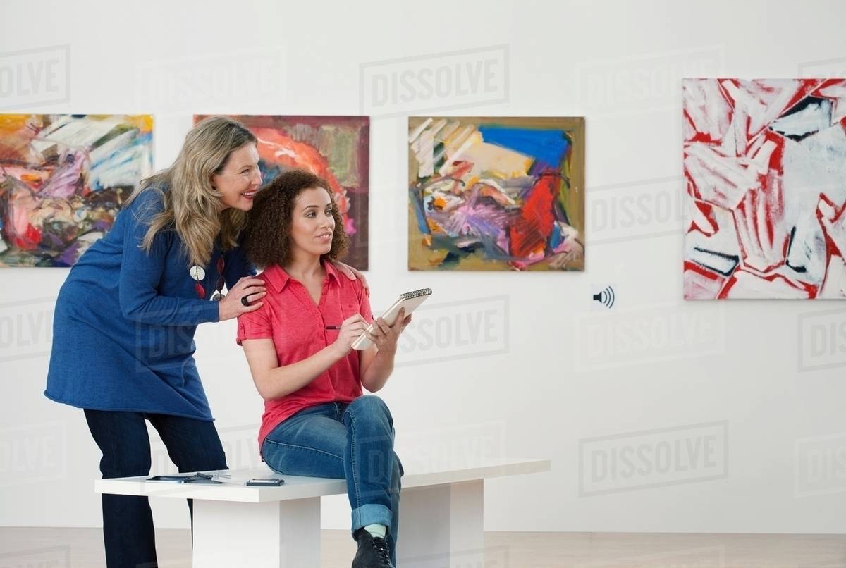 Mid adult woman advising art student drawing in sketch pad in art ...