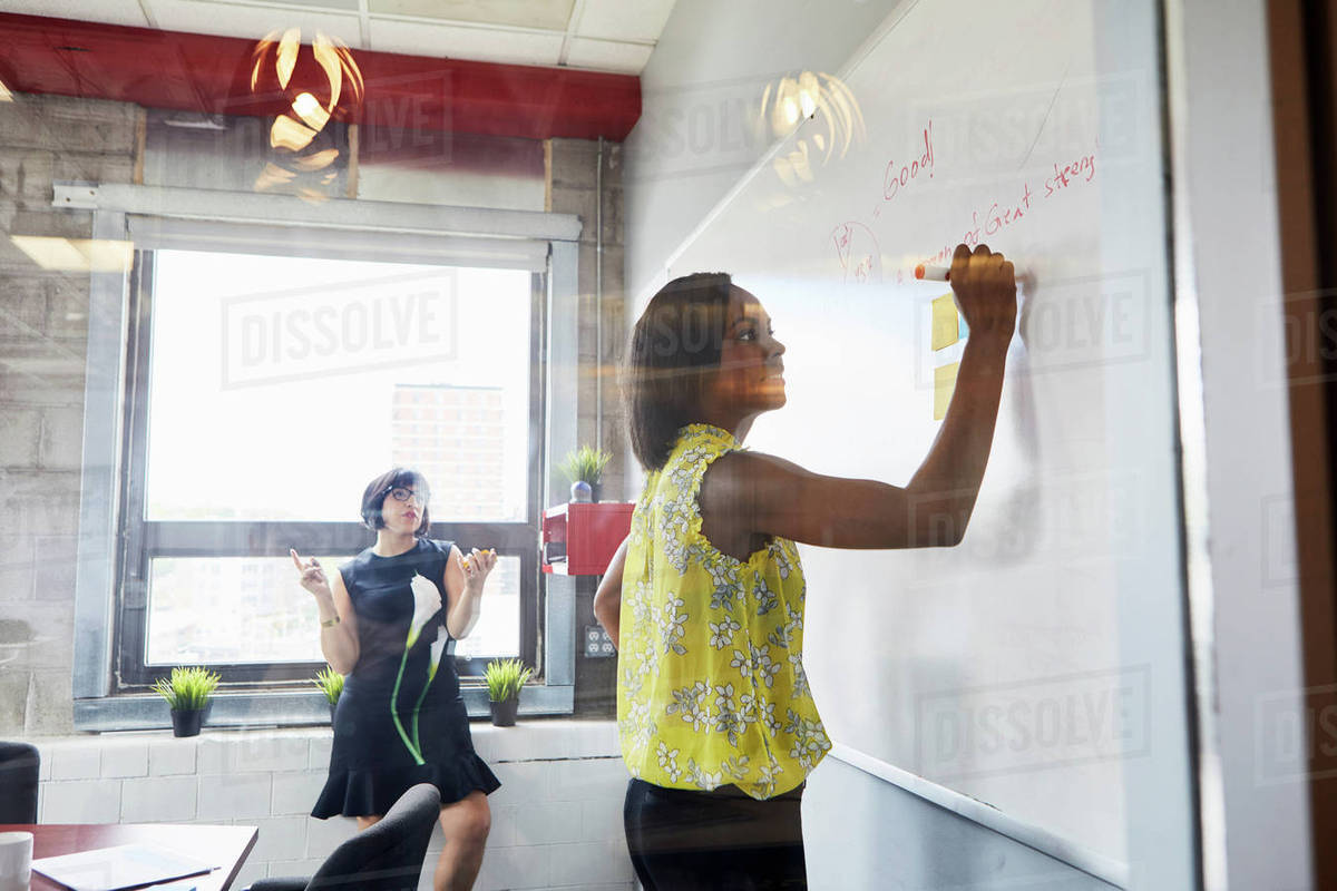 Two women in office, solving problem, using whiteboard, sticky notes ...