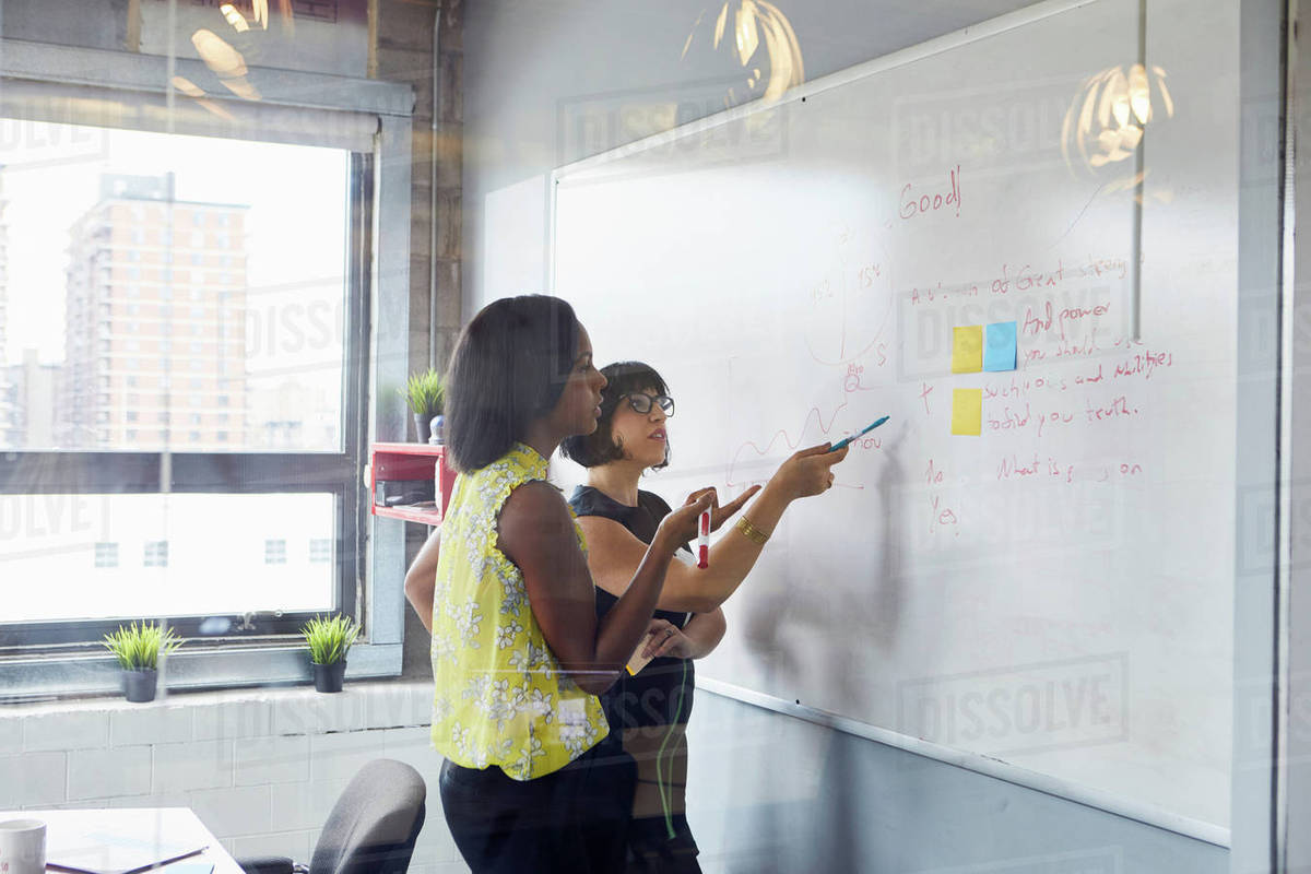 Two women in office, solving problem, using whiteboard, sticky notes ...