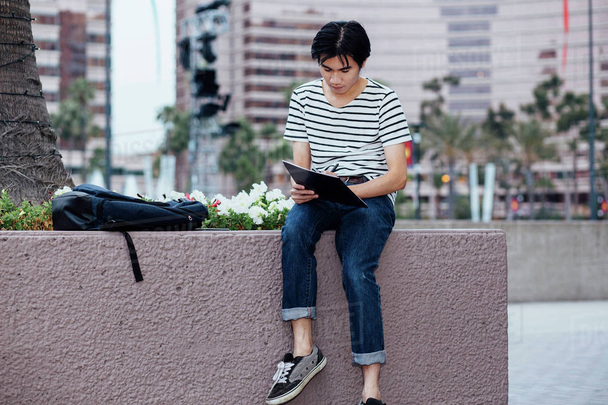 Young man sitting on wall, outdoors, writing in notebook - Royalty-free ...