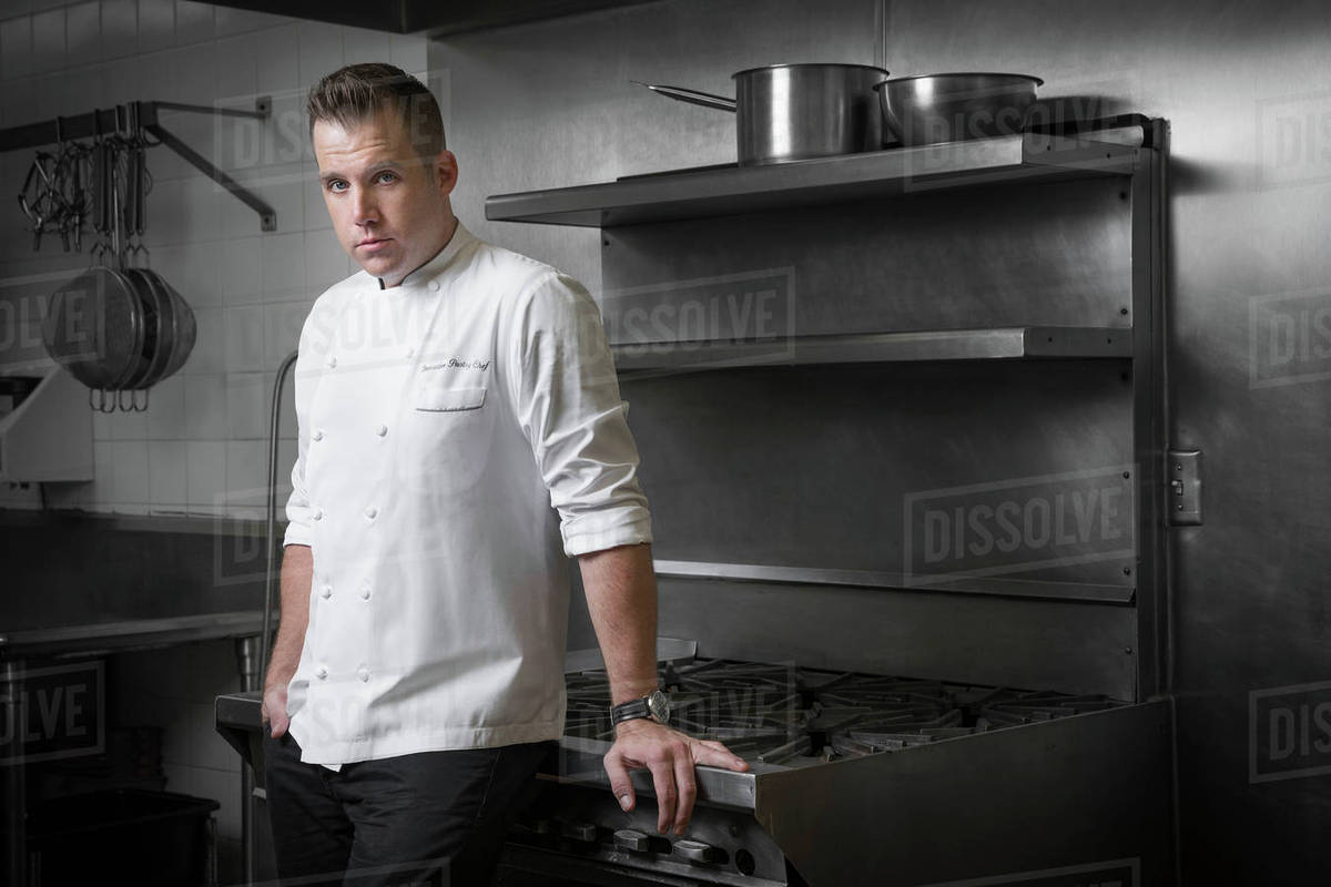 Portrait of pastry chef leaning against hob in kitchen - Royalty-free ...