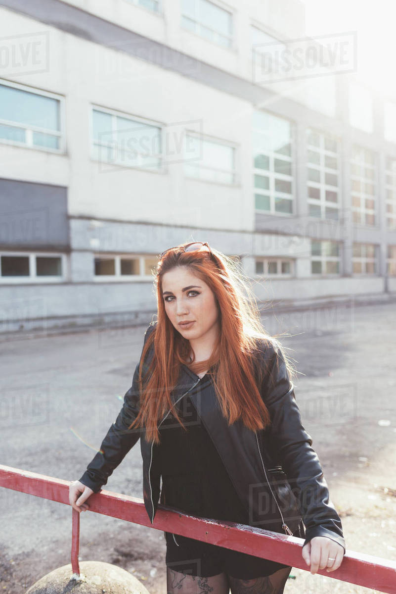 Portrait of red haired woman leaning against railing looking at camera ...