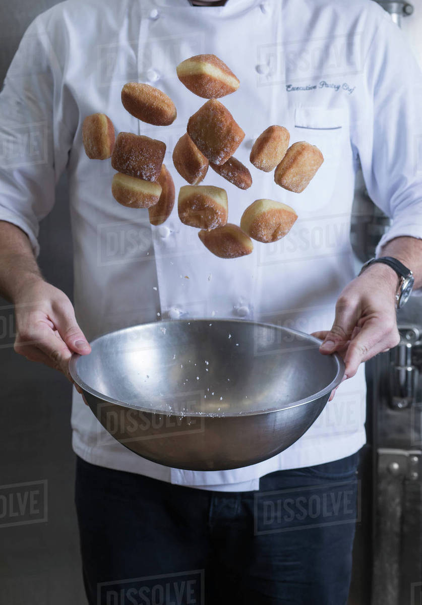 Cropped view of chef tossing doughnuts and sugar in mixing bowl ...