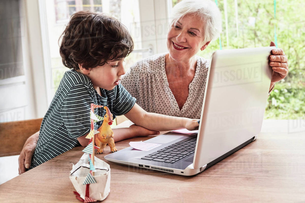Grandmother and grandson sitting at table, using laptop - Royalty-free ...