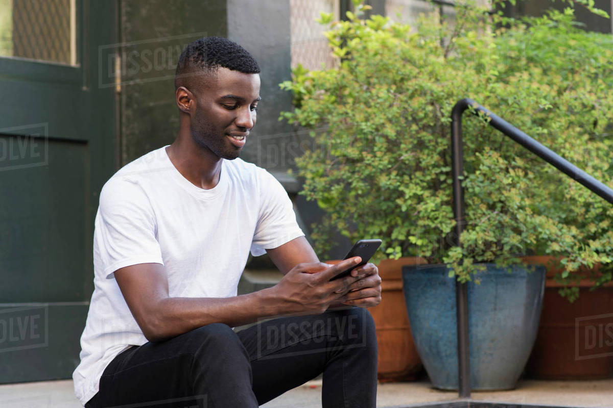 Young man using cellphone on step in streets of New York, US - Royalty ...