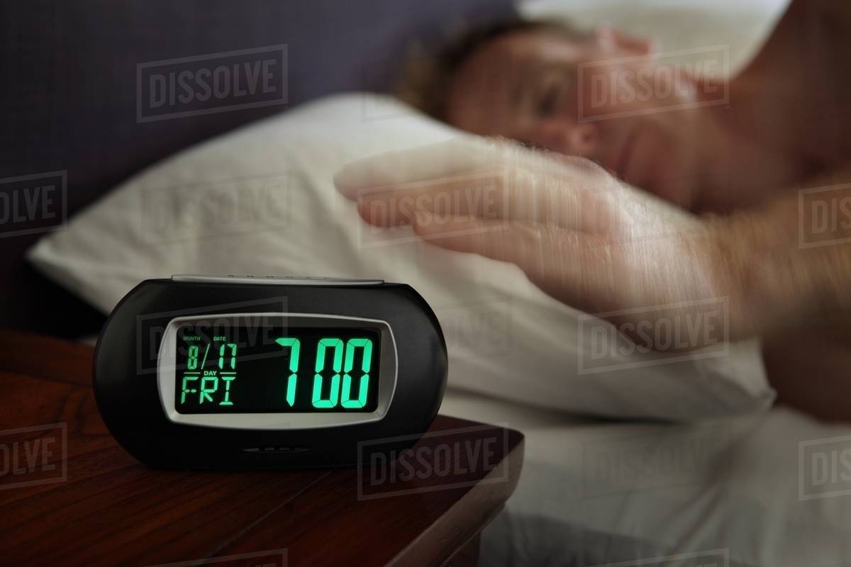 Man reaching for alarm clock - Stock Photo - Dissolve